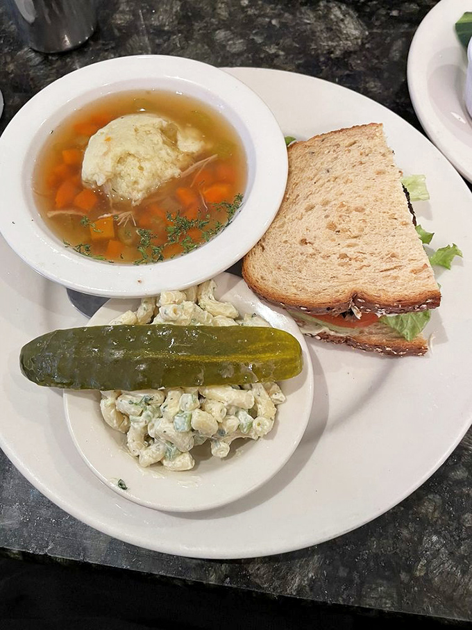 The ultimate power lunch: matzo ball soup, sandwich, and pickle—a trio so perfect they should tour together like rock stars.