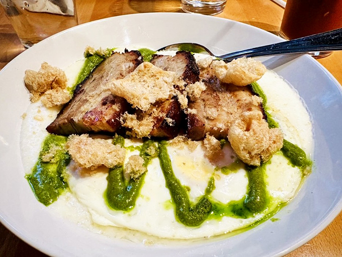 Pork belly resting on a cloud of grits with vibrant green sauce&mdash;proof that breakfast can be both comforting and sophisticated, like wearing slippers with a tuxedo.