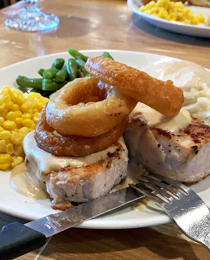 Not to be outdone by its feathered friend, the pork chop arrives like a heavyweight champion, crowned with crispy onion rings.
