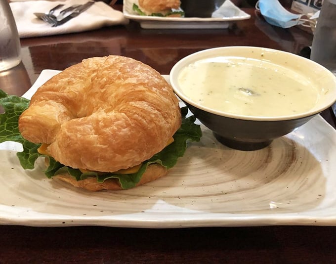 That croissant sandwich isn't just lunch&mdash;it's architecture. Flaky, buttery layers cradle fresh greens while that soup whispers, "Dip me, you know you want to."