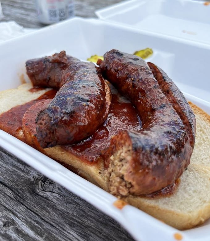 The sausage link, glistening with sauce, sits like barbecue royalty atop its throne of white bread.