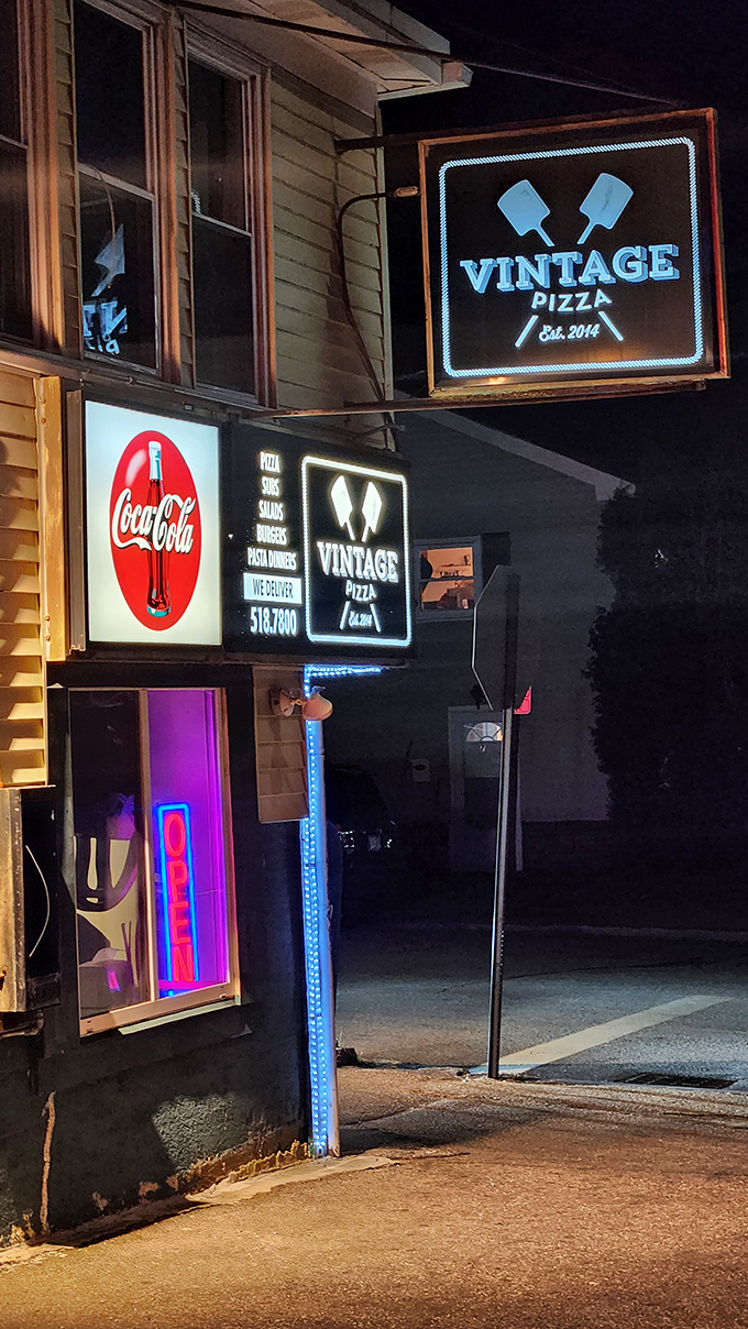By night, the neon glow transforms this modest takeout spot into a beacon for those seeking pizza salvation.