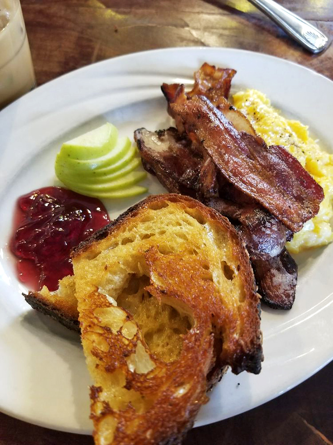 The breakfast trinity: perfectly crisped bacon, golden toast, and scrambled eggs that actually taste like eggs. Add apple slices and jam for that "yes, this is technically healthy" feeling.