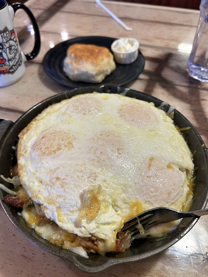 Breakfast skillet magic: eggs floating atop a treasure chest of potatoes and savory delights. The biscuit stands guard, ready for gravy duty.
