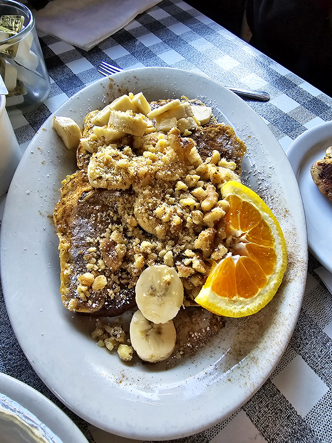The French toast looks like it's auditioning for a dessert menu, sporting banana slices, crushed walnuts, and enough powdered sugar to leave evidence on your shirt.