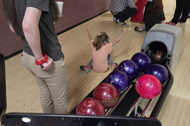 The moment of childhood triumph captured&mdash;arms raised in victory as colorful bowling balls await their turn to create more memories.