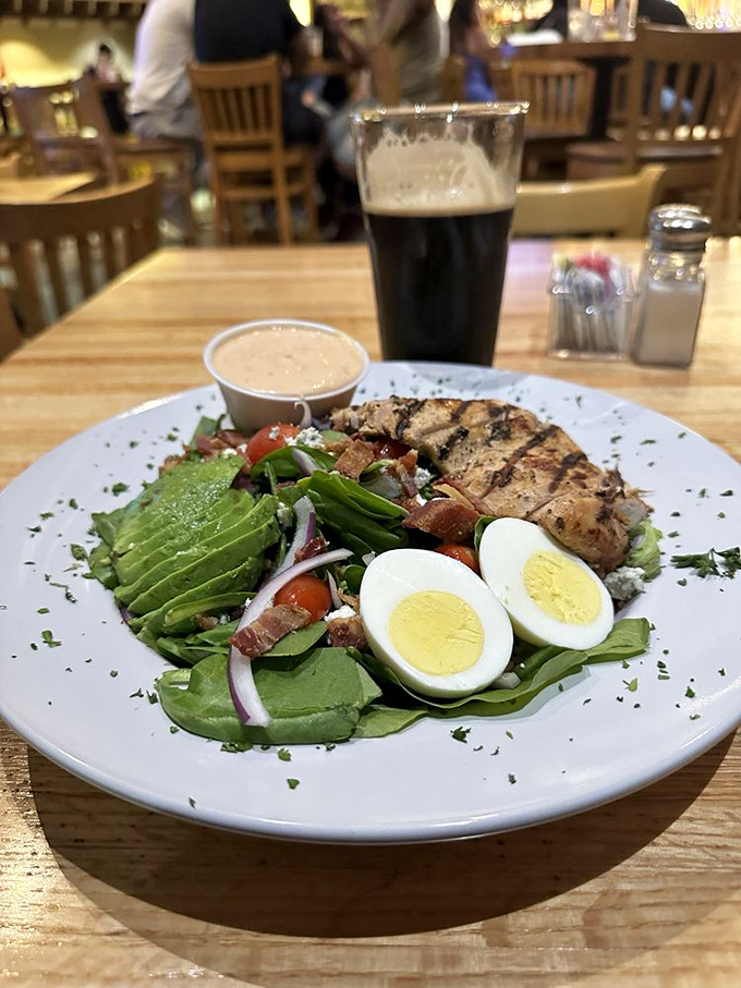 When a salad looks this good, even dedicated carnivores pause. Grilled chicken, avocado, and egg atop fresh greens with dark beer alongside.