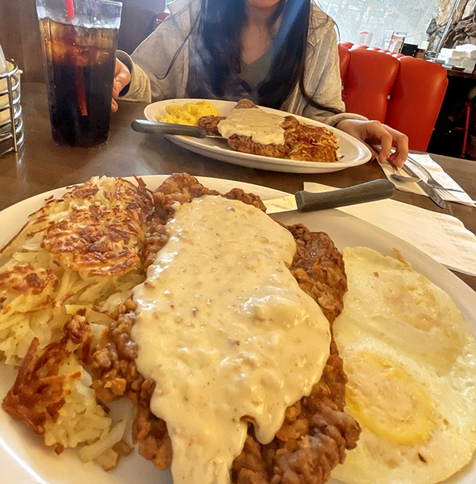 Country fried steak swimming in gravy like it's taking a delicious spa day, with hash browns standing by as fluffy golden lifeguards.