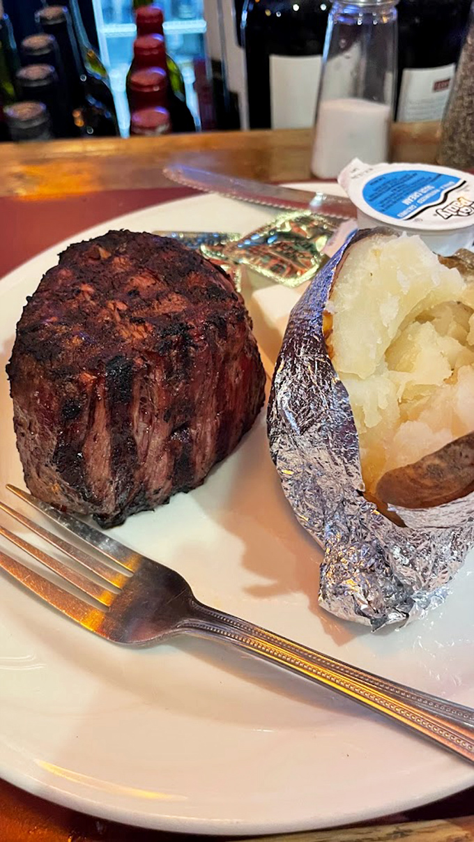 The filet mignon stands like a delicious monument to beef perfection, while the potato waits patiently in its silver jacket.