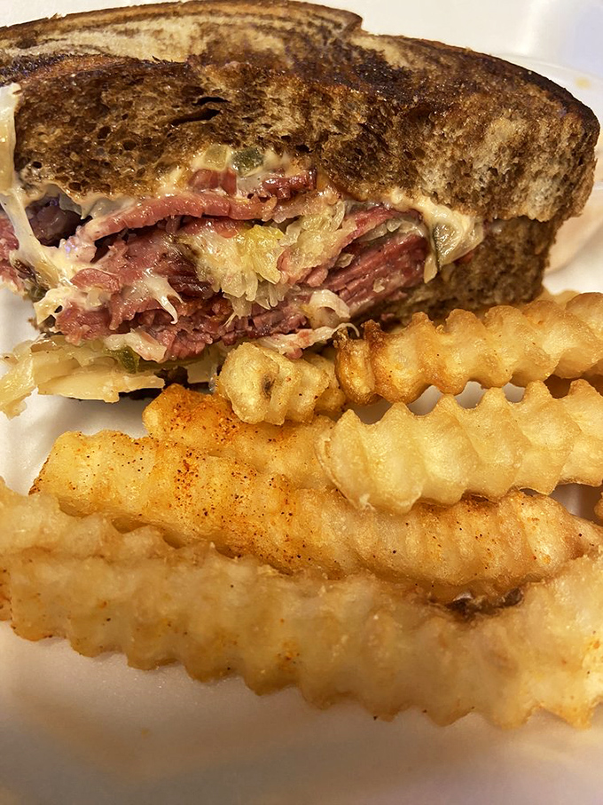The Reuben sandwich stands tall and proud, layers of corned beef and sauerkraut nestled between grilled bread with those crinkle-cut fries playing perfect wingman.