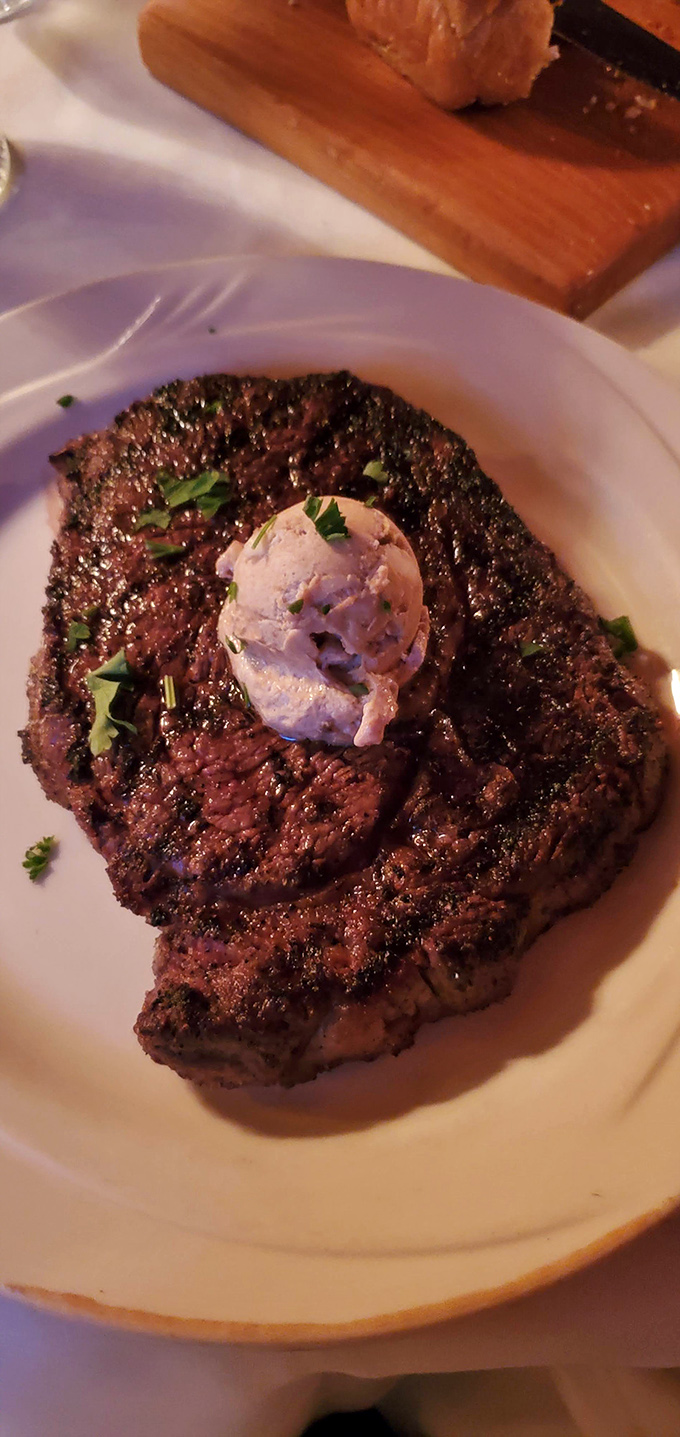 The perfect steak wears its char like a badge of honor, crowned with compound butter slowly melting into beef perfection.