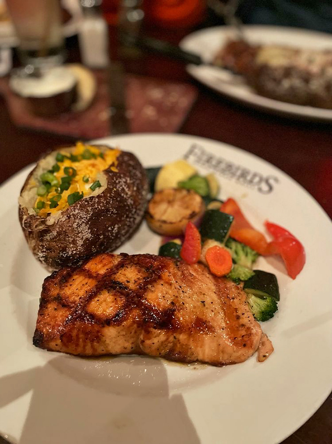 Salmon with perfect grill marks flanked by a loaded baked potato and fresh vegetables. The holy trinity of a satisfying dinner.