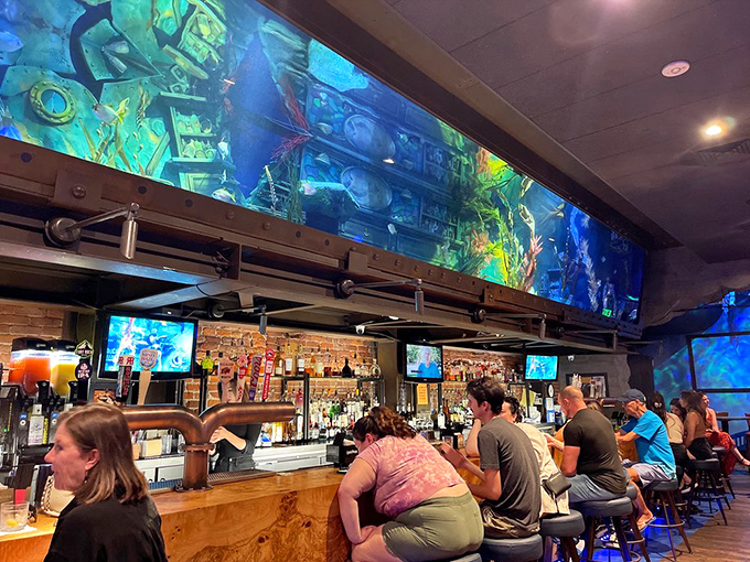 The massive aquarium tank stretches above the bar, creating an immersive underwater experience. Like drinking inside a kaleidoscope filled with seawater.