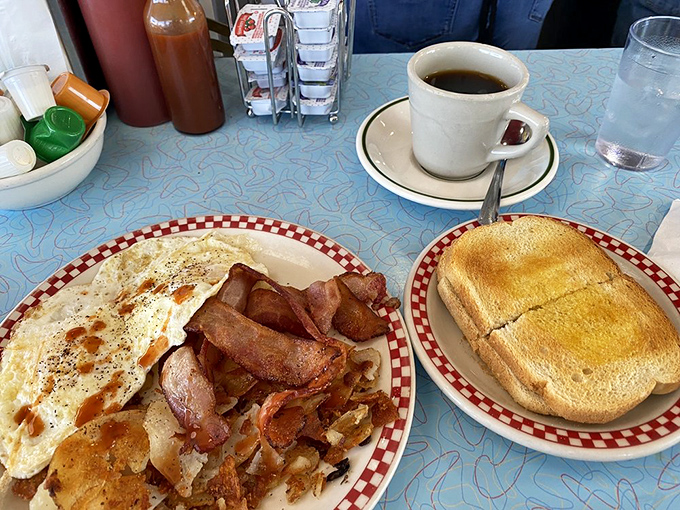 The breakfast holy trinity: scrambled eggs that look like clouds, crispy hash browns with perfect browning, and a sausage patty waiting to complete the morning symphony.