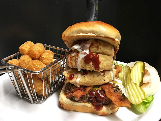 A towering burger achievement that defies both gravity and hunger, complete with a basket of golden tots that demand equal attention.