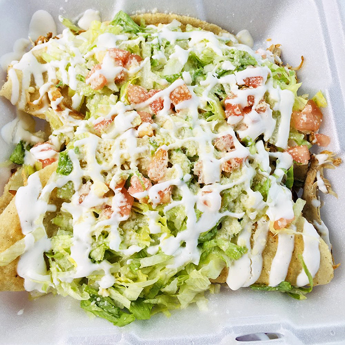 A mountain of nachos that could feed a small village, crowned with the holy trinity of lettuce, tomato, and sour cream.