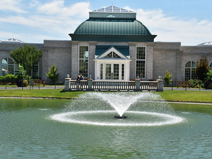The conservatory stands guard behind a fountain that dances with sunlight. Architecture and water performing their daily duet.