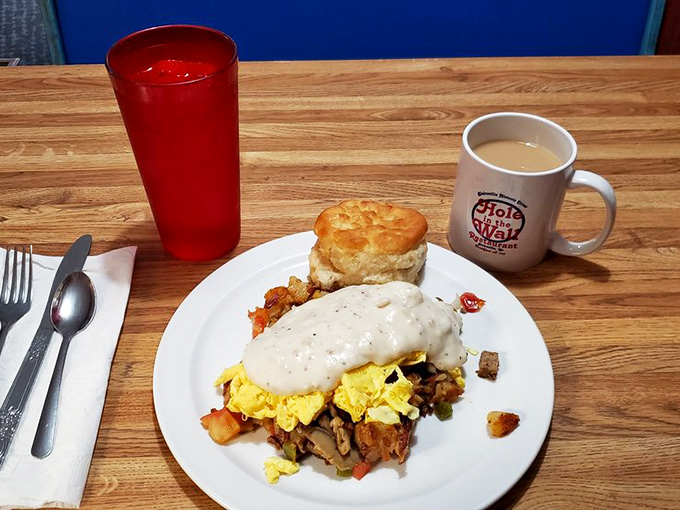 The holy breakfast trinity: strong coffee in a branded mug, hearty food smothered in gravy, and a biscuit standing tall like a Southern monument.