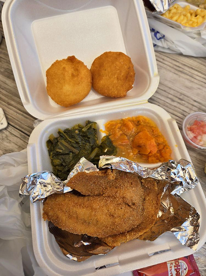 Two perfect hushpuppies stand guard over greens and sweet potatoes like sentinels protecting the treasure of perfectly fried fish below.