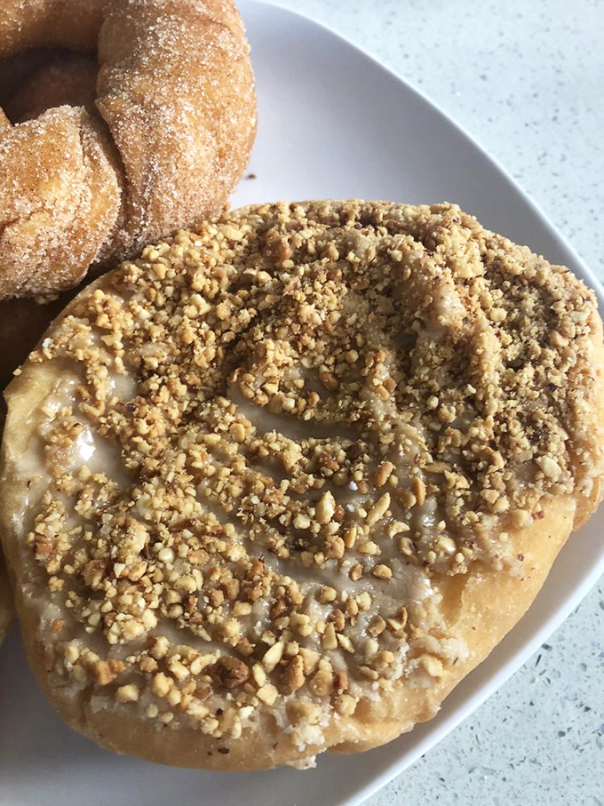 The peanut caramel donut offers a textural masterpiece—crunchy topping yielding to soft dough beneath. A symphony in every bite.