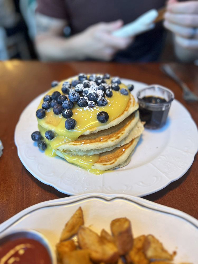 Pancakes wearing blueberries like crown jewels, swimming in lemon curd that's bright enough to replace your morning coffee.
