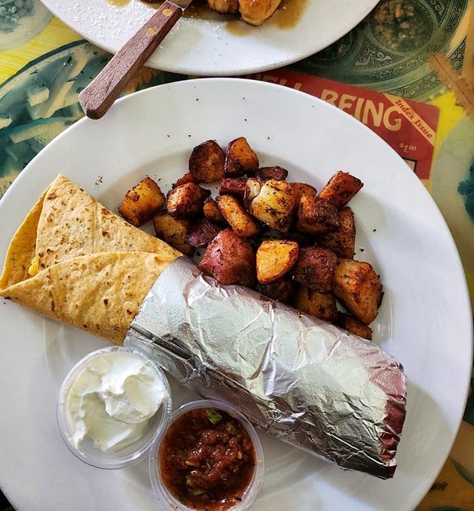 The holy trinity of breakfast bliss: hearty burrito wrapped in foil, crispy potatoes, and all the necessary accompaniments for a morning fiesta.