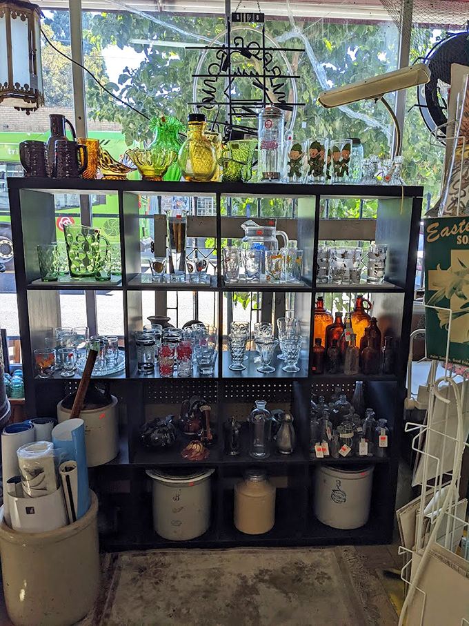 Sunlight transforms colored glassware into a stained-glass cathedral of cocktail hour. Each shelf a different decade, each piece a conversation starter.