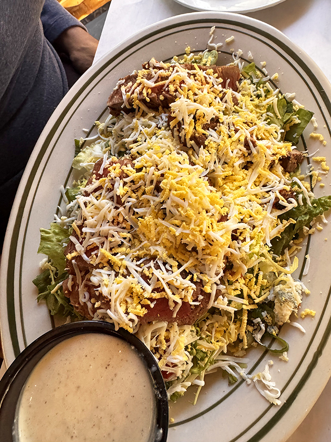 A steak salad that cleverly disguises indulgence as virtue, with cheese and protein playing hide-and-seek among innocent lettuce leaves.