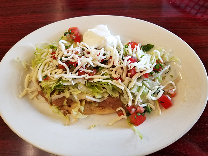 This tostada is architecture on a plate—crispy foundation supporting layers of flavor, crowned with fresh veggies and cheese that make every bite a textural adventure.
