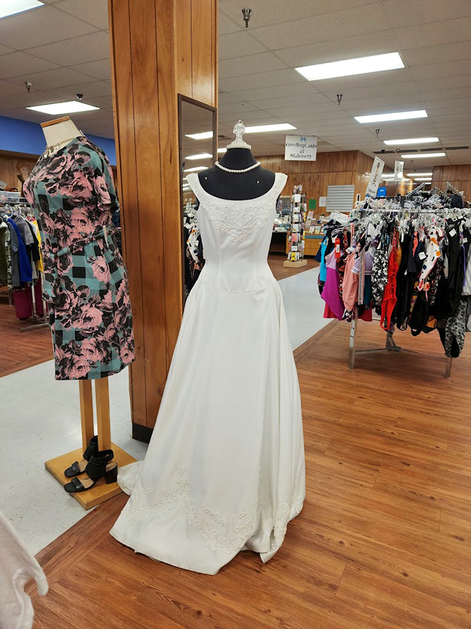 A pristine wedding gown stands sentinel among everyday clothes, whispering of one perfect day and awaiting its next walk down the aisle.