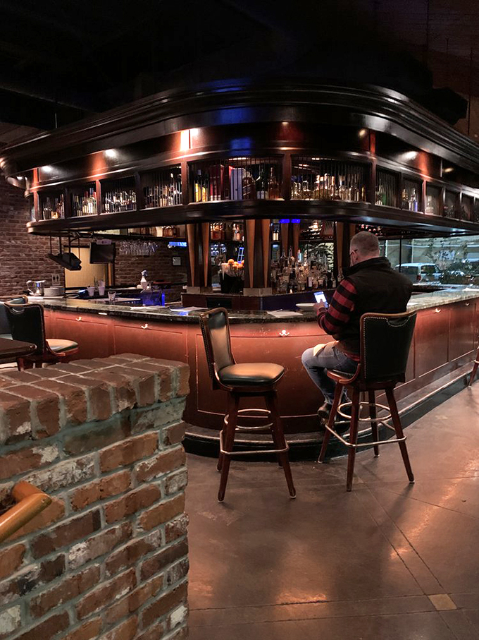 The curved bar, backlit bottles, and warm wood tones create the kind of atmosphere where strangers become friends and nobody's counting how many Manhattans they've had.