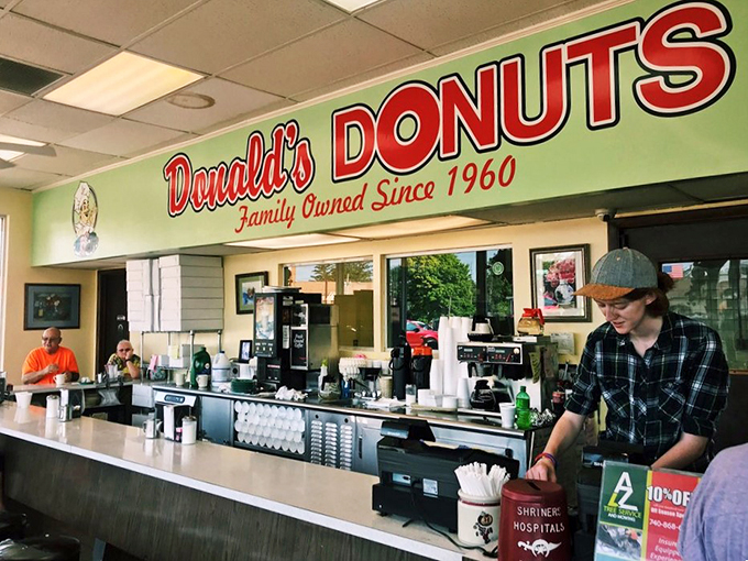 Behind this counter, donut magic happens daily. The green and red signage watching over decades of sweet transactions and morning rituals.
