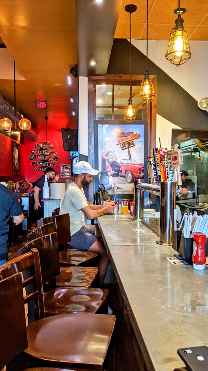 Where the magic happens—industrial pendant lights illuminate the bar where locals gather to witness burger artistry in progress.