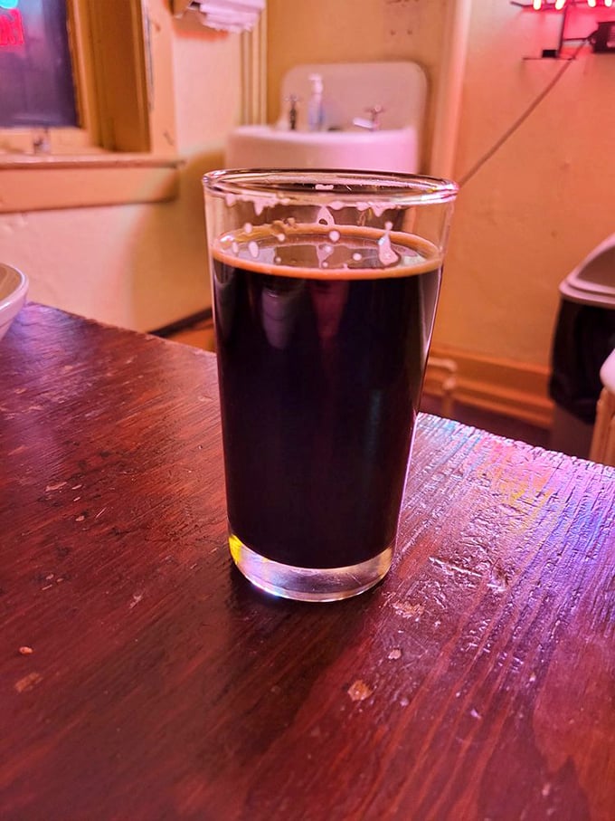 A proper pint of dark beer sitting on a worn wooden bar&mdash;sometimes the simplest pleasures are the ones we travel furthest to find.
