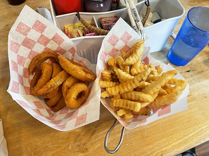 The dynamic duo of comfort food sides—crinkle-cut fries and onion rings—served in checkered paper baskets that signal deliciousness ahead.