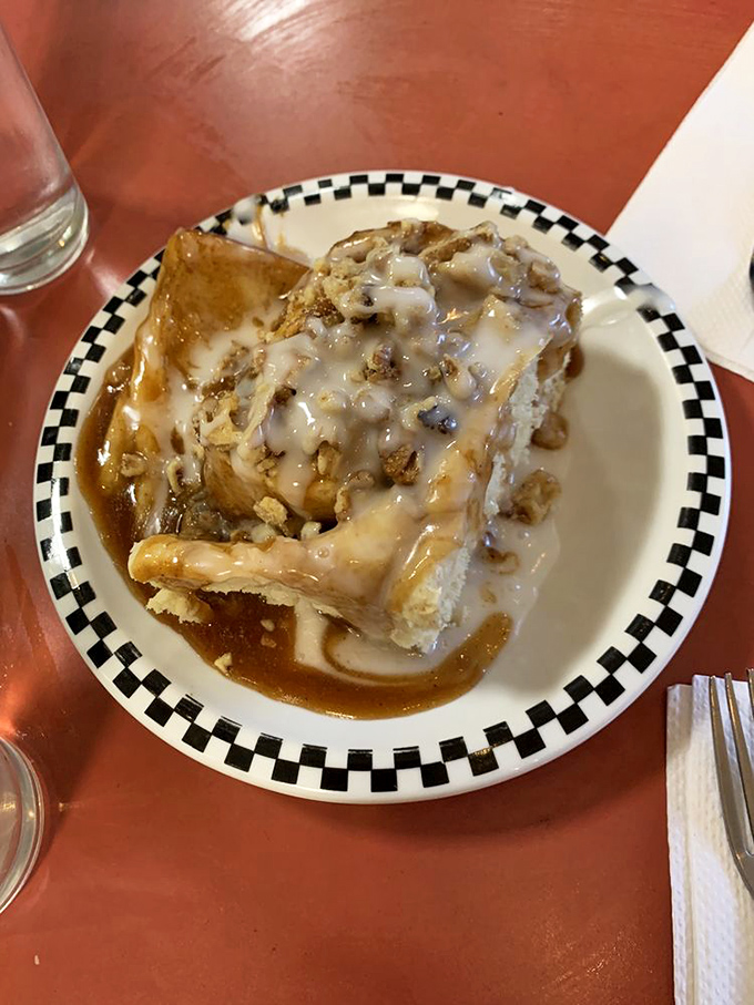 A cinnamon roll wearing a nutty crown sits in a pool of caramel. Some foods deserve their own throne, and this is definitely one of them.