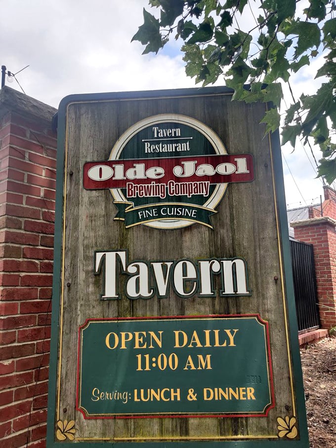 The weathered wooden sign stands like a sentinel, promising fine cuisine where once stood a house of correction.