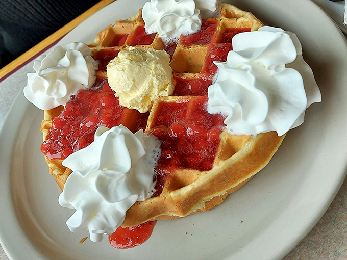 A Belgian waffle adorned with strawberry sauce and whipped cream mountains&mdash;breakfast that boldly crosses into dessert territory without a passport.