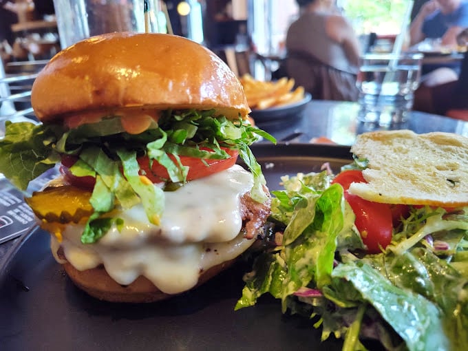 A burger so perfectly stacked it belongs in an architecture textbook, with layers of fresh veggies and melty cheese creating a skyscraper of flavor.