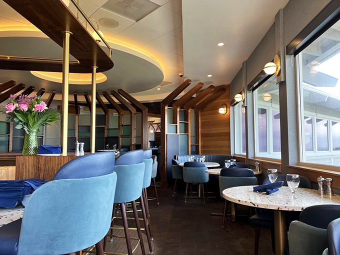 Blue velvet booths and woven pendant lights create the nautical-chic atmosphere that makes you feel both sophisticated and ready for barefoot beach walks.