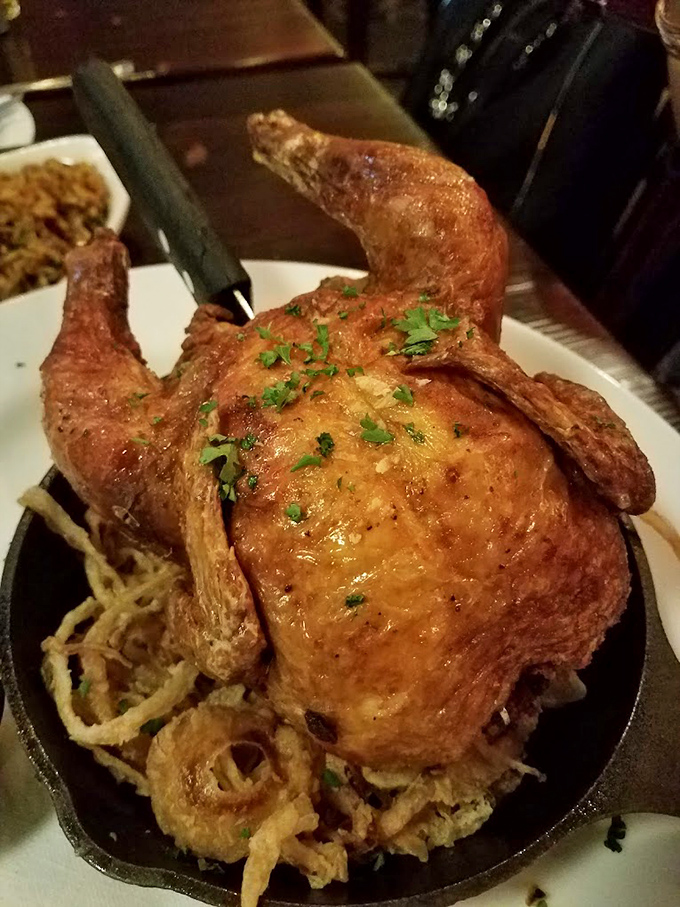 A whole roasted chicken perched on crispy onion strings like a throne &ndash; royalty of comfort food with herb-flecked skin that shatters on contact.