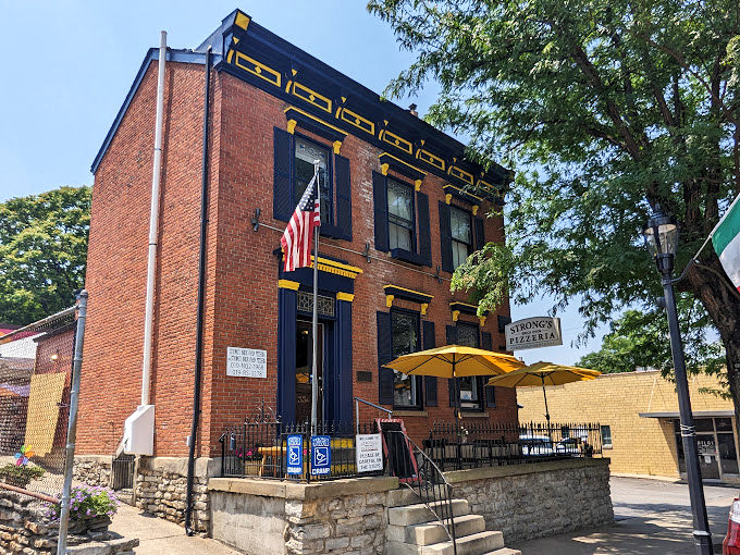Those blue shutters and American flag frame a building where pizza traditions are both honored and reinvented.