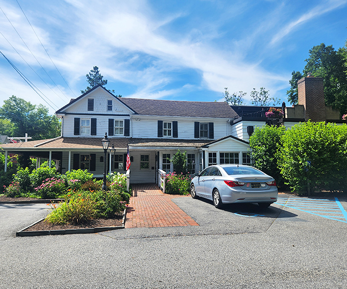 The historic white clapboard exterior of Buckley's Tavern welcomes visitors with lush greenery and brick pathways, a Delaware landmark since the 1700s.
