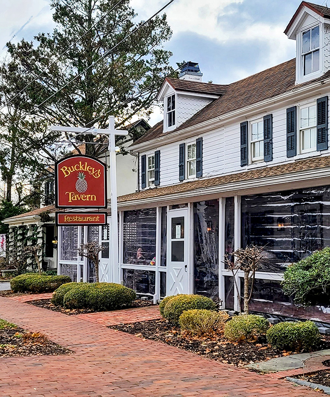 The historic white clapboard exterior of Buckley's Tavern welcomes visitors with lush greenery and brick pathways, a Delaware landmark since the 1700s.