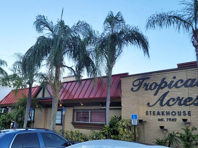 The unassuming exterior of Tropical Acres Steakhouse, where palm trees stand guard over Florida's best-kept carnivorous secret since 1949.