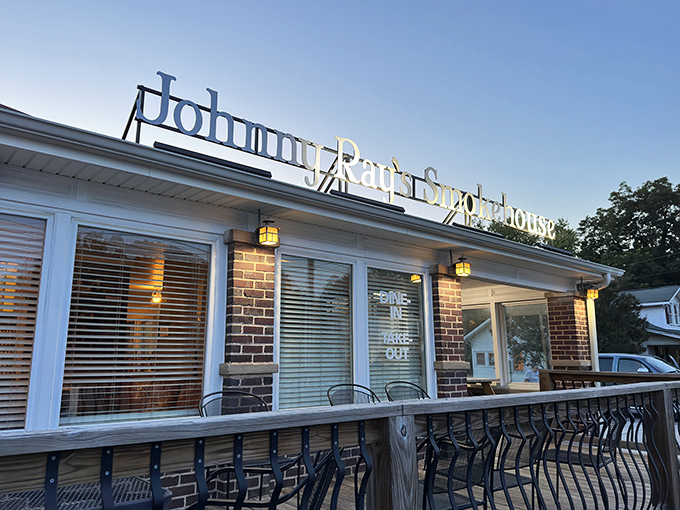 The welcoming glow of Johnny Ray's Smokehouse beckons hungry travelers with its homey brick exterior and cozy wooden deck&mdash;barbecue paradise found. 