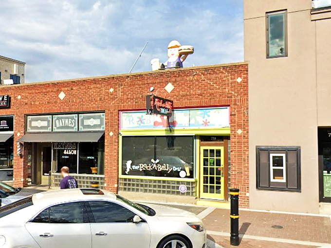 The bright yellow door acts like a portal to flavor town, with that whimsical sandwich figure on the roof standing guard over culinary treasures below.