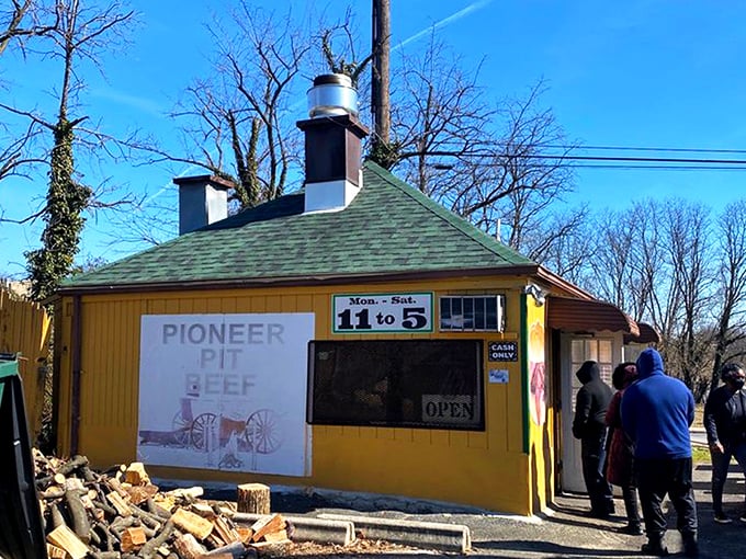 The humble yellow shack with stacked firewood speaks volumes: real pit beef doesn't need fancy digs when the smoke does the talking.