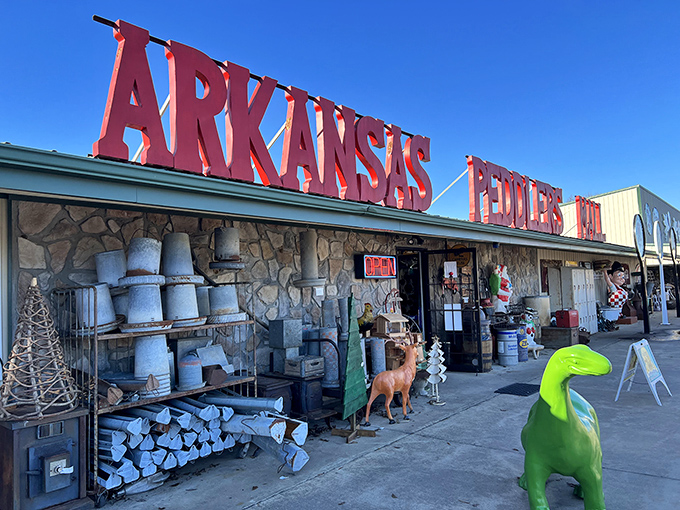 The bright red letters of Arkansas Peddlers stand like a welcoming carnival barker against the sky, with that charming green dinosaur keeping watch over vintage treasures.