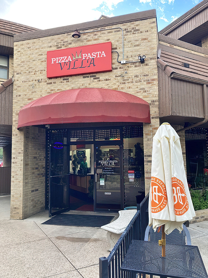 The inviting brick exterior with its cheerful red awning promises Italian delights within. Purple flowers and lush greenery create a welcoming oasis in Denver.